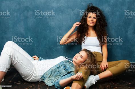 若いかわいい十代の少女の友人 ブロンドとブルネットの巻き毛は青い背景に陽気なポーズライフスタイルの人々の概念 2人のストックフォトや画像を