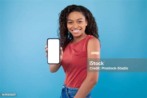 온라인 코로나바이러스 예방 접종 앱용 모형이 있는 빈 스마트폰을 보여주는 접착제 붕대를 가진 젊은 흑인 여성 건강관리와 의술에 대한 스톡 사진 및 기타 이미지 Istock