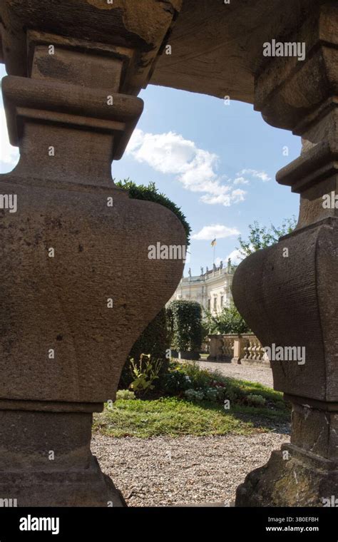 Two Large Stone Balusters Frame A View Of A Green Garden With A Building In The Background