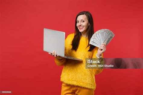 노란 털 스웨터 노트북 Pc 컴퓨터 달러 지폐 현금 돈 빨간 배경에 고립에 돈의 팬을 들고 웃는 젊은 여자 사람들이 감정 라이프 스타일 개념 복사 공간을 비웃는 다 가을에
