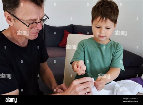 Father Teaching His Son How To Sew On A Button Shot At Home Stock