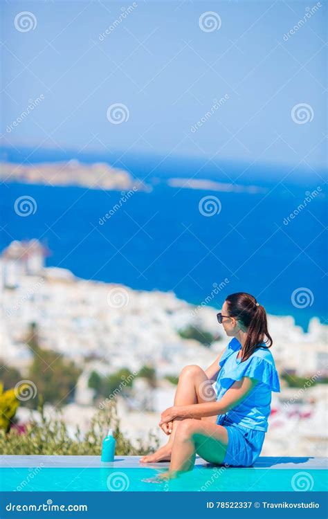 Slim Woman Applying Sunscreen On Her Legs Sitting On The Edge Of Pool