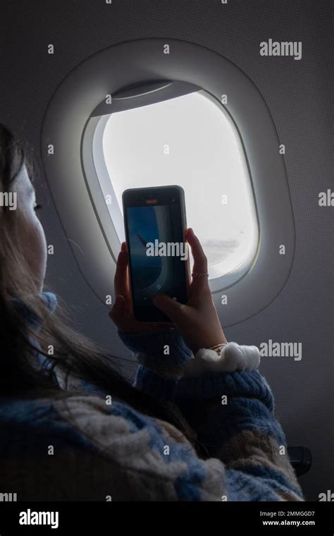 Young Girl Sitting At The Window Seat On Airplane While Taking Pictures