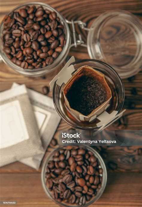 집에서 커피를 만드는 추세 갈색 배경에 커피 원두가 든 유리잔에 신선한 음료가 담긴 가방을 드립한다 컵에 양조하기위한 분쇄 커피 용지 필터를 사용하여 커피를 드립합니다