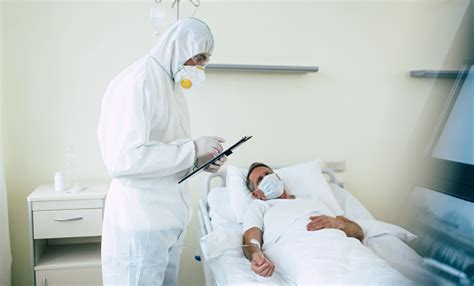 성인 남성 환자는 병원 병동에 있는 침대에 누워 있으며 보호복과 마스크를 착용한 의사의 검사를 받았습니다 2명에 대한 스톡 사진