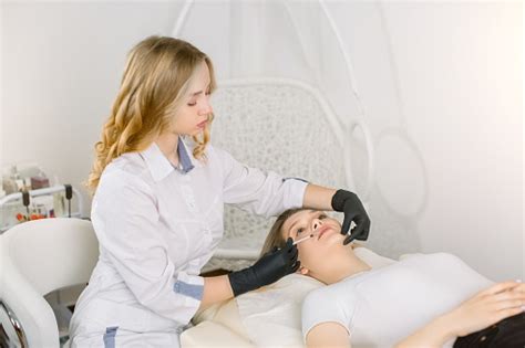 예쁜 젊은 백인 금발 소녀 소파에 누워 뷰티 주사를 받고 여성 미용사는 여성의 입술에 노화 방지 주사를 합니다 젊어짐과 뷰티