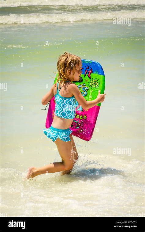 Young Little Blonde Girl In Bathing Suit Runs In The Surf Along The