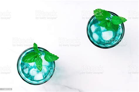 차가운 음료와 얼음 조각이있는 두 개의 아름다운 빈티지 청록색 안경 흰색 대리석 테이블에 신선한 녹색 민트 잎으로 장식 0명에