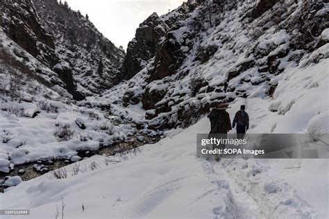 Men Walk Along A Snow Covered Path Next To A Frozen Stream During A