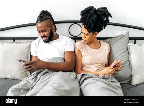 African American Married Couple Sit In A Cozy Bed Use Their