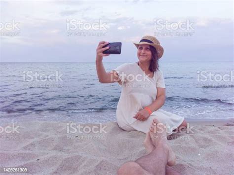 한 남자가 해변에서 쾌활한 여성이 바다와 하늘을 향해 셀카를 찍는 사진을 찍습니다 휴가에 대한 스톡 사진 및 기타 이미지