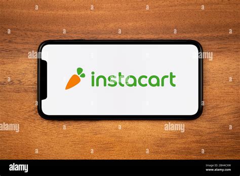 A Smartphone Showing The Instacart Logo Rests On A Plain Wooden Table