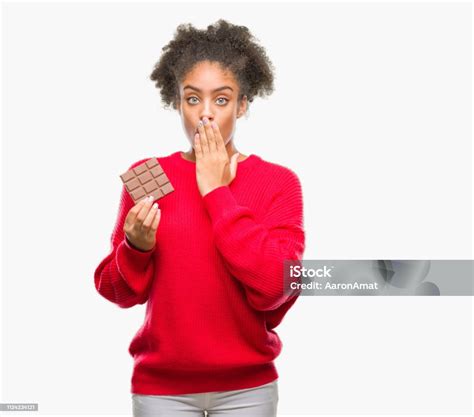 격리 된 배경 표지 입 손으로 이상의 초콜릿을 먹는 젊은 아프리카 미국 여 자가 실수 두려움 침묵 비밀 개념에에서 무서 워의 표현에 대 한 수치와 충격 가리기에 대한 스톡