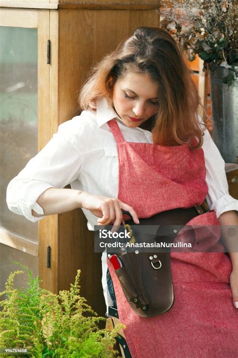 젊은 귀여운 레이디 핑크 린 넨 앞치마 흰 장갑과 플로리스트 도구 가죽 벨트를 착용 하는 온실에서 일하고 일 날 개념 후 휴식 가지치기 가위에 대한 스톡 사진 및 기타