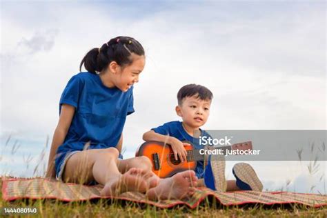 야외에서 노는 사랑스러운 형제와 자매의 초상화 정원에서 노래를 부르는 아시아 아이들 야외에서 즐거운 시간을 보내는 기타를 가진
