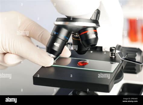 Scientist Examining Sample Of Red Liquid On Slide Under Microscope In