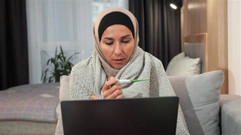 Sick Muslim Woman Wrapped In A Blanket Looks At The Thermometer Feel