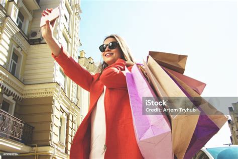 Selfie 시간입니다 붉은 코트와 선글라스 쇼핑 가방 Selfie 복용에 명랑 하 고 매력적인 여자의 초상화 푸른 하늘 배경입니다 가방에 대한 스톡 사진 및 기타 이미지