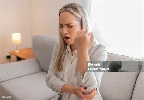 팔 통증이있는 여성 실내에서 고통스러운 손을 마사지하는 여성 팔꿈치 통증으로 고통받는 팔꿈치를 들고있는 여성의 손 집에서 고통을