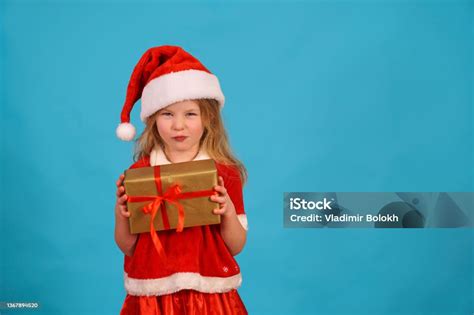 산타 클로스 모자에 재미 크리스마스 어린이 소녀는 선물 얼굴을 잡고있다 얼굴 표정으로 재생합니다 선물로 만족하는 소녀의 슬리 룩 장난꾸러기와 장난 꾸러기 와 선물 에 블루