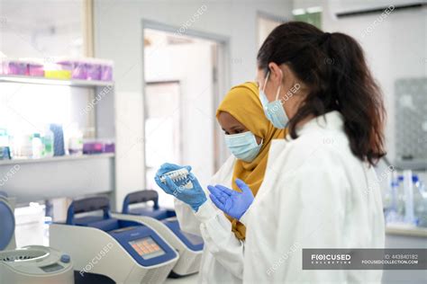 Female Scientists In Face Masks With Specimen Holder In Laboratory