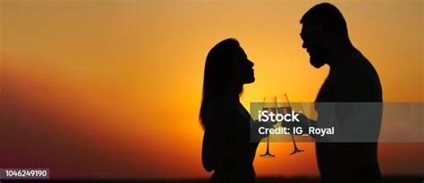 남자와 웃 고 샴페인 그들의 손에 잔을 들고 몇 낭만적인 날짜 설정 서로 와인잔을 홀 짝 일몰 극적인 하늘 배경에서 여자의 실루엣 2명에 대한 스톡 사진 및 기타 이미지