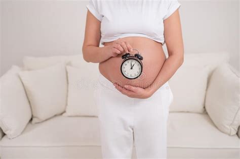 A Pregnant Woman With A Naked Belly Holds An Alarm Clock Intended Date