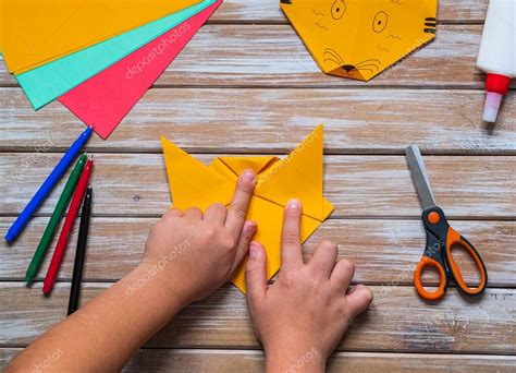 El niño pliega el origami Tigre paso a paso del papel naranja sobre un fondo de madera Símbolo
