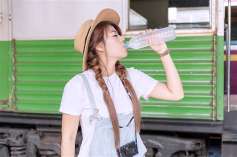 여행자 젊은 여성은 기차역에서 누군가를 기다리는 동안 그녀의 손에 신선한 물 양식 병을 마시는 카메라와 모자를 착용 라이프