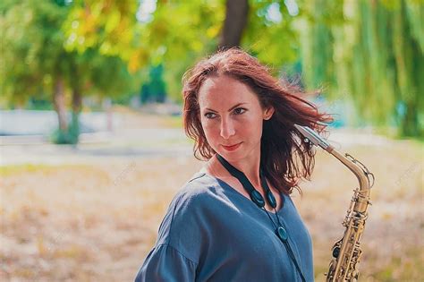 A Stunning Redhead With A Saxophone Captured In An Intimate Portrait Amidst Lush Greens Photo