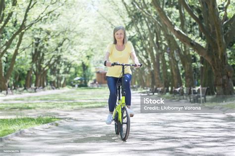 활동적인 라이프 스타일 시니어 아름다운 스포티 한 여성은 야외에서 공원에서 노란색 자전거를 타고 그는 가고 카메라를보고 미소 지었다 55 59세에 대한 스톡 사진 및 기타