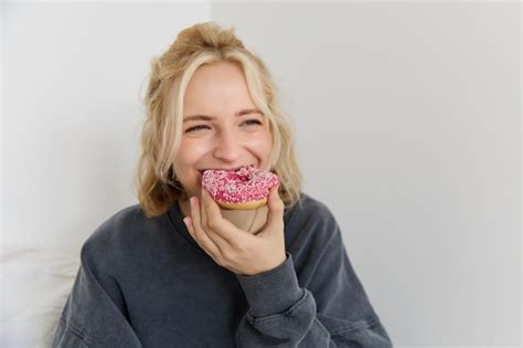 Retrato En Primer Plano De Una Feliz Mujer Rubia Con Una Rosquilla En La Mano Comiendo Comida