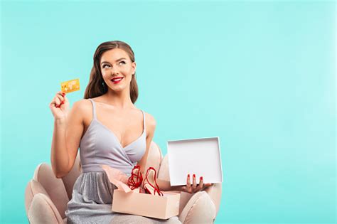 쇼핑 여성 20 대 는 파란색 배경에 고립 된 안락 의자에 앉아있는 동안 신발과 신용 카드와 선물 상자를 들고 드레스에 20 대
