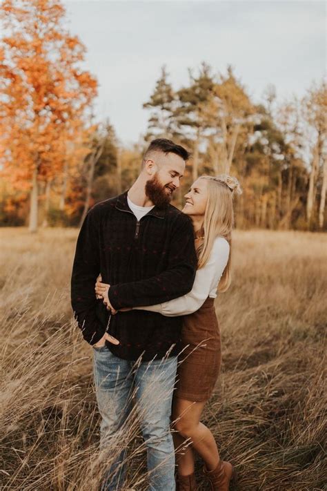 A Man And Woman Standing In Tall Grass With Their Arms Around Each