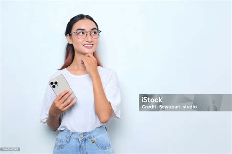 스마트폰을 들고 흰색 티셔츠를 입은 호기심 많은 젊은 아시아 소녀의 초상화 흰색 배경에 격리된 복사 공간을 바라보고 있다 20