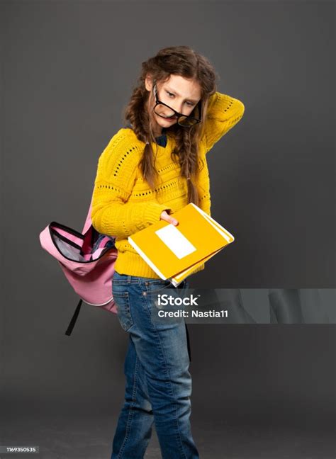 분홍색 배낭을 들고 안경을 쓴 여학생의 전체 길이 초상화와 패션 스타일의 의류에서 회색 스튜디오 배경을 내려다 보는 피곤 학교로 돌아갑니다 가득 찬에 대한 스톡 사진 및