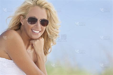 美丽的金发女人穿着白裙子和太阳镜在海滩上