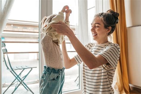 Madre Amorosa Vistiendo A Su Hija Junto A La Ventana Foto Premium
