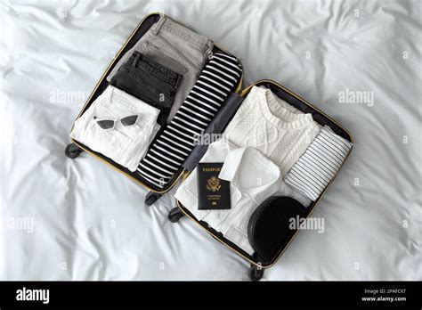 Open Suitcase With Clothes Passport And Accessories On Bed Top View
