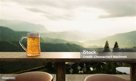 나무 테이블과 의자 세트에 넣어 상단에 맥주 거품이있는 투명 유리에 초안 또는 공예 맥주 신의 빛이나 햇빛이 있는 나무 테라스의 라운지 좌석3d 렌더링 맥주에 대한 스톡