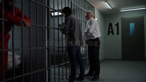 Prison Officer Locks Criminal In Orange Uniform In Jail Cell Stock