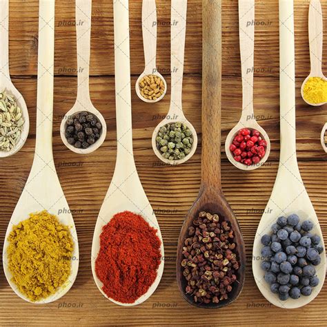 عکس ادویه های متفاوت در قاشق های کوچک و بزرگ چوبی در پس زمینه چوبی