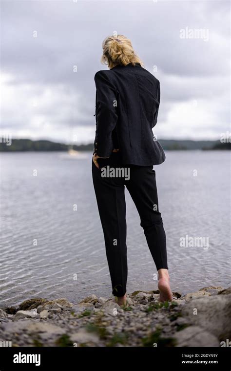 A Back View Of A Cool Barefoot Woman In A Black Suit Standing Near A