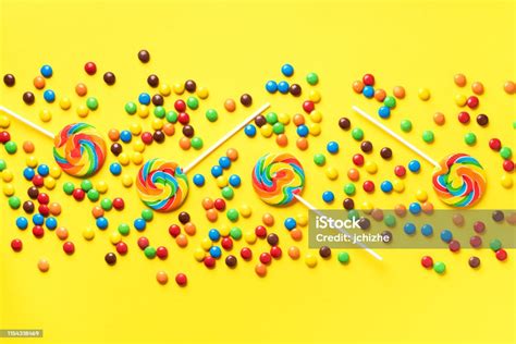 여러 가지 빛깔의 롤리팝 노란 배경에 무지개 다채로운 사탕 코팅 된 초콜릿 달콤한 조각 질감입니다 평면도 평평한 누워 휴일