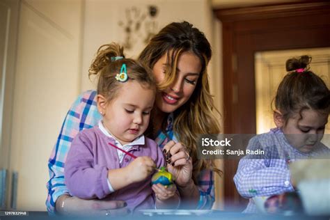 엄마는 그녀와 그녀의 여동생이 부활절 달걀을 색칠 할 때 무릎에 그녀의 막내 아이를 들고있다 2 3 살에 대한 스톡 사진 및 기타 이미지 Istock