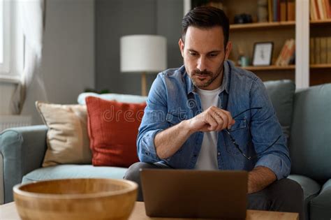 Focused Male Computer Programmer Holding Eyeglasses And Working Over Laptop Seriously While