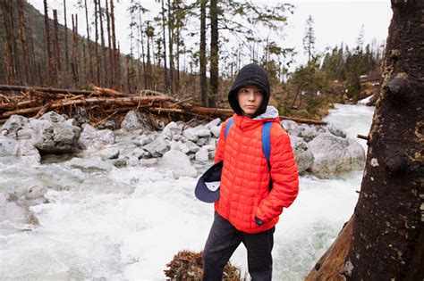 빨간 재킷과 까마귀에 있는 십 대 소년은 슬로바키아의 높은 타트라 산맥에서 비오는 추운 날에 산 강 옆에 서 있습니다 십대 소년에 대한 스톡 사진 및 기타 이미지 Istock