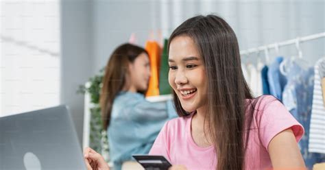 아시아 비즈니스 여성은 창고의 웹 스토어에서 온라인 쇼핑을 즐깁니다 젊은 매력적인 사업가들은 테이블에 앉아 일하고 사용 후 전자 은행 온라인 지불을 만들기 위해 신용