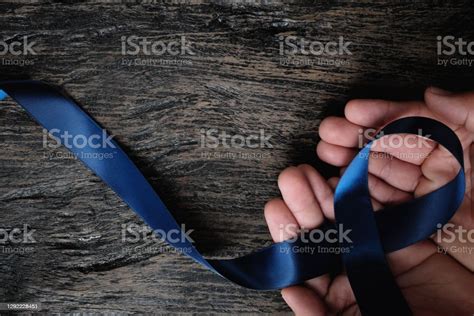 복사 공간이있는 나무 배경에 어두운 파란색 리본을 들고 있는 남성 손의 상단 보기 결장 위 대장암 관절염 급성 호흡 곤란 증후군