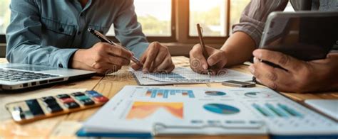 Two Colleagues Working Together At A Desk Analyzing Financial Data And Charts With Laptops